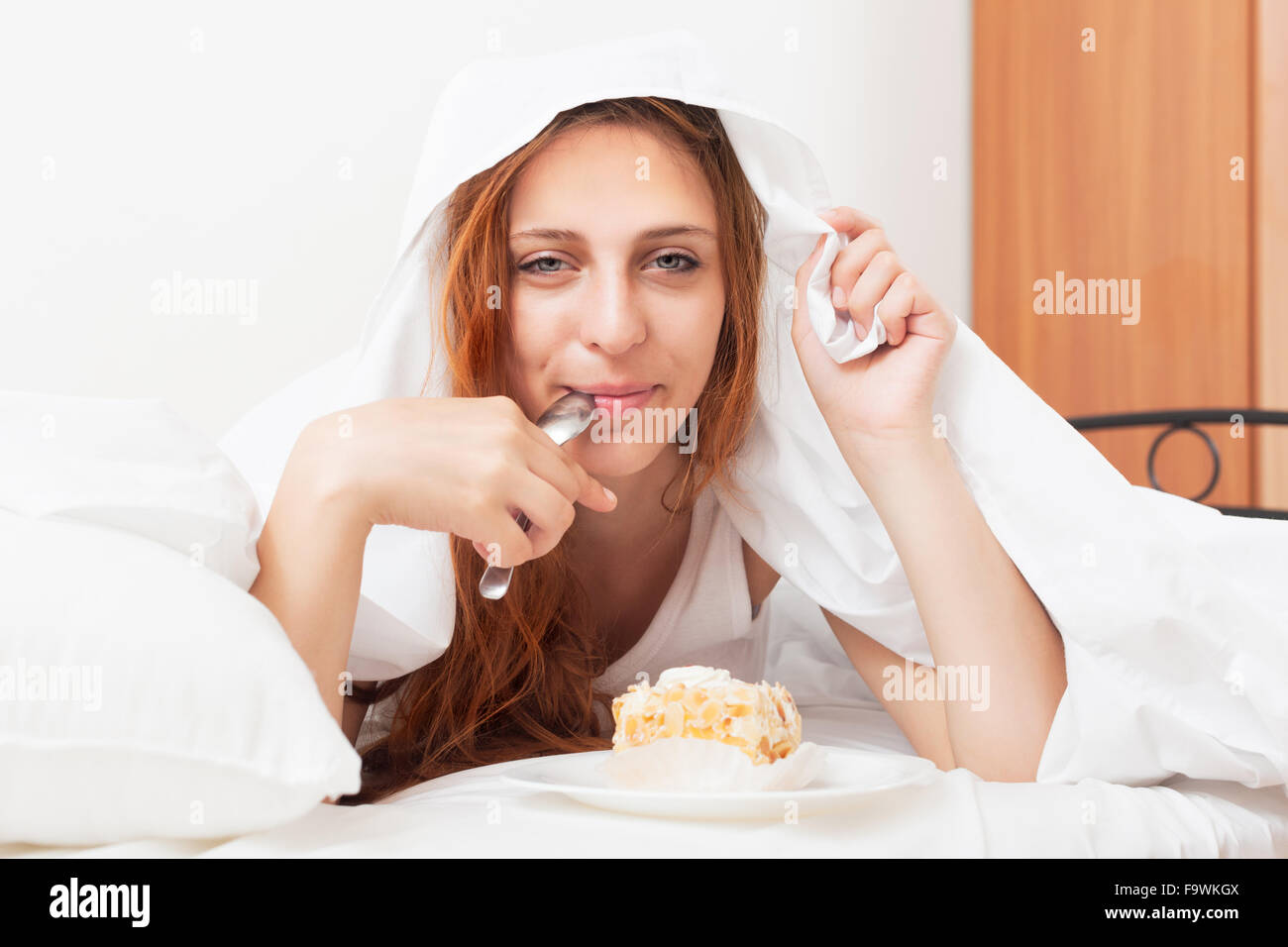 Beautiful woman eating sweet cake under sheet in bed at home Stock ...