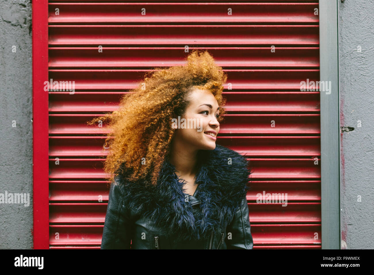 Ireland, Dublin, smiling woman with afro in front of red roller shutter ...