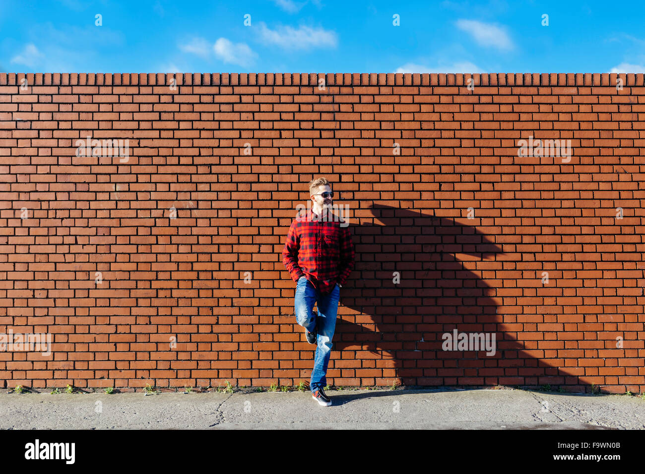 Young man leaning against brick wall Stock Photo - Alamy