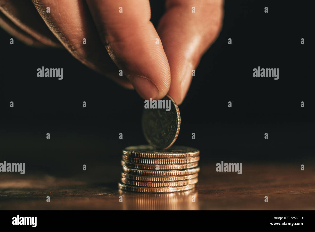 Hand holding coin on top of stack of coins Stock Photo - Alamy