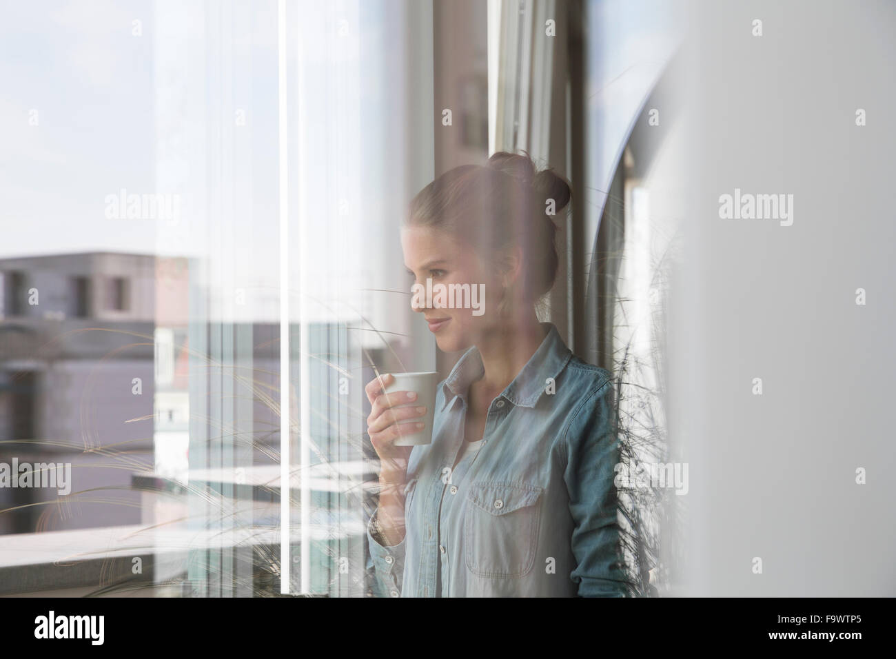 Young woman standing at the window, drinking coffee Stock Photo - Alamy