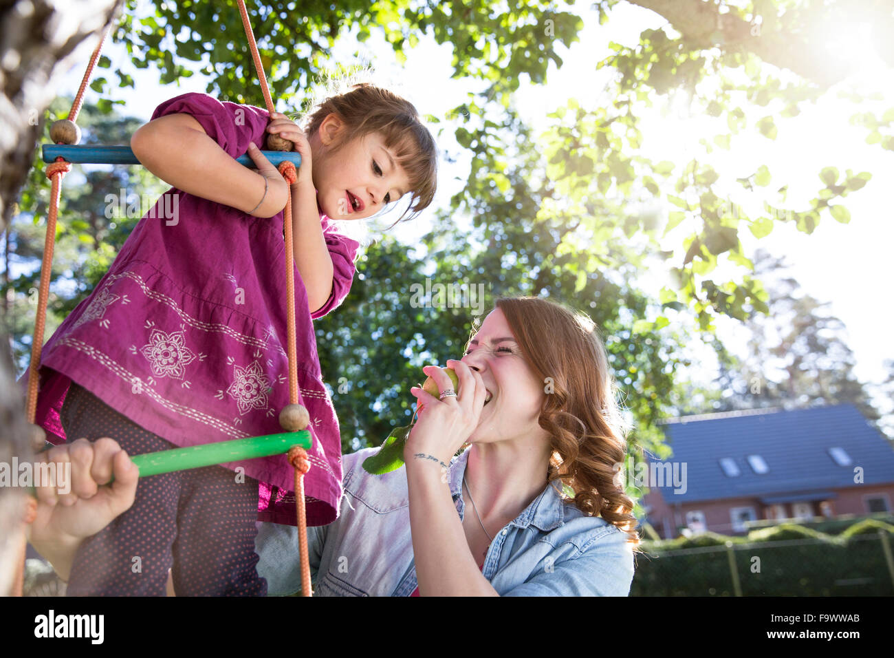 Mother eating an apple with daughter on rope ladder in garden Stock ...