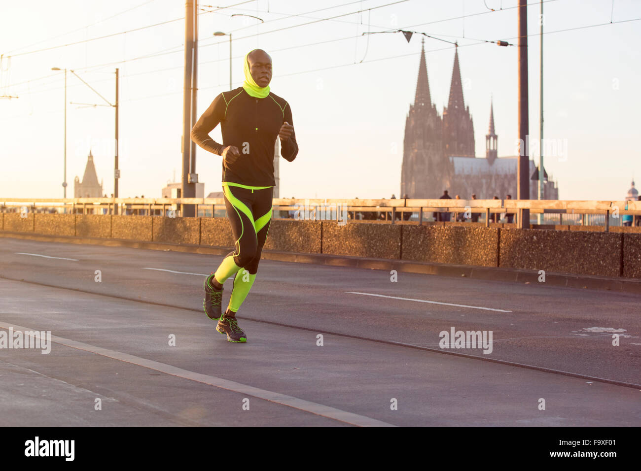 Germany, Cologne, athlete running on bridge with Cologne Cathedral in ...