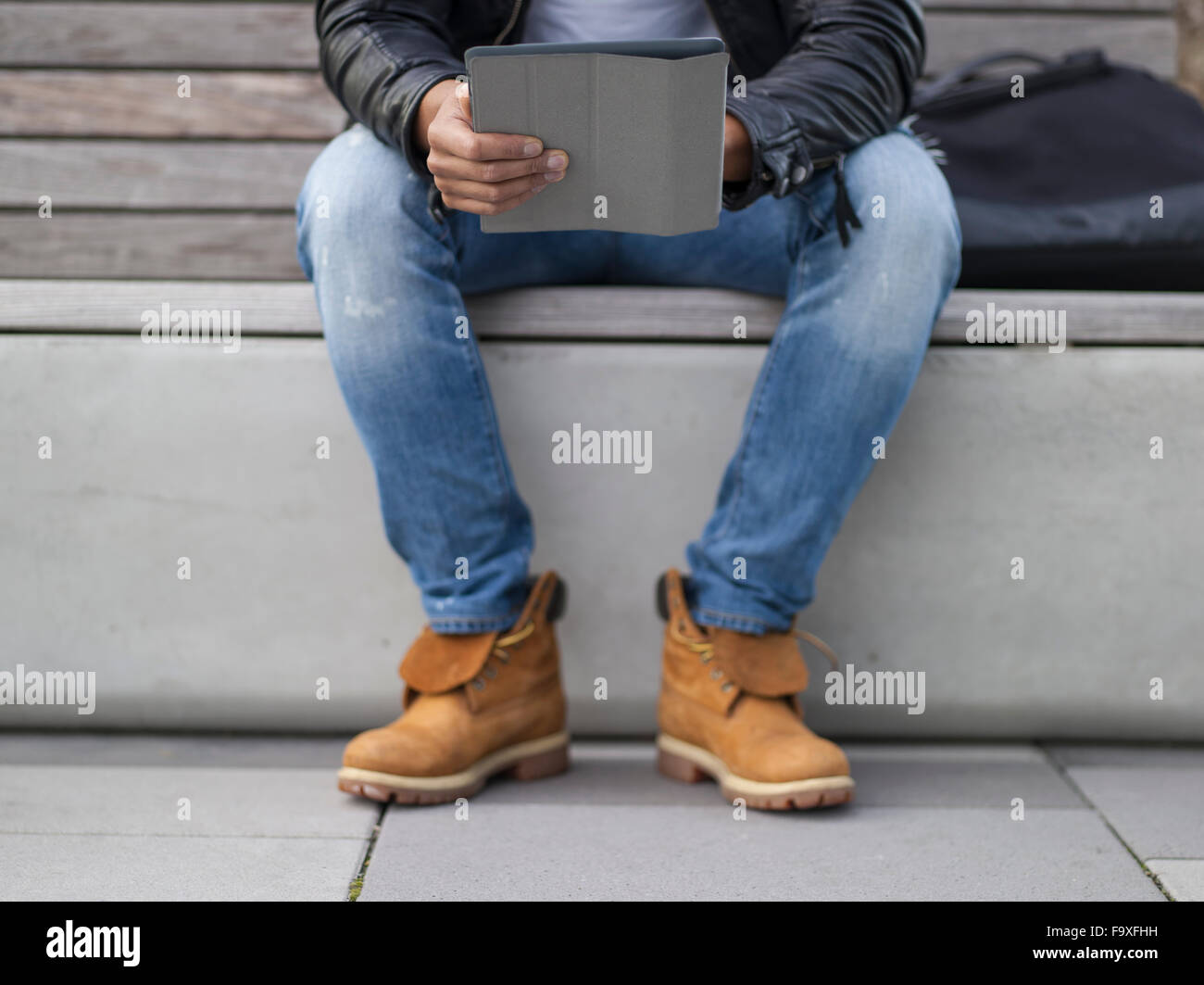 Germany, Cologne, Young man sitting on bench using digital tablet Stock ...
