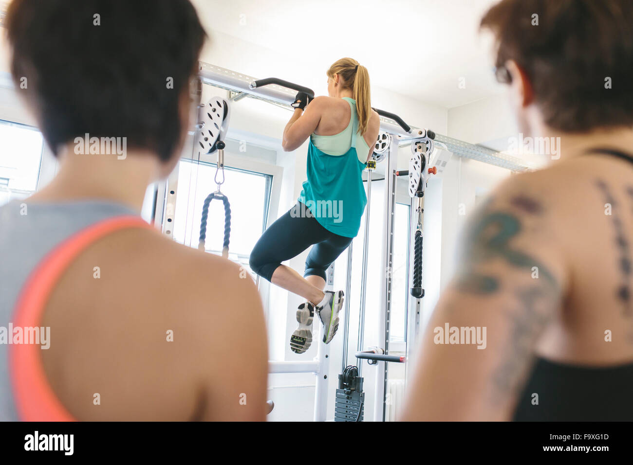 Two women watching athlete doing pull-ups in gym Stock Photo - Alamy