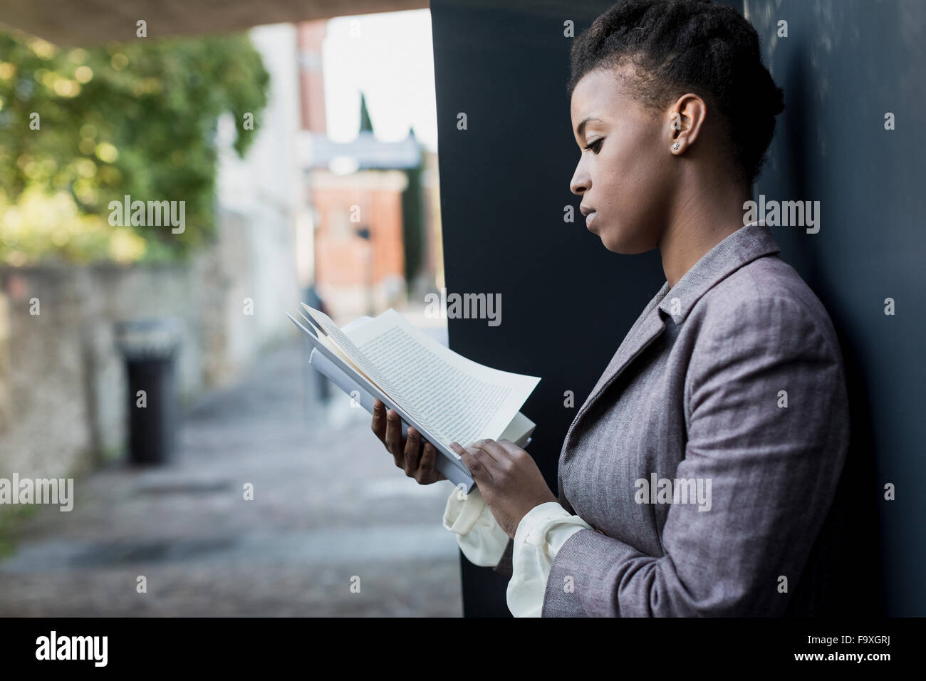 Young woman leaning against wall reading a book Stock Photo - Alamy