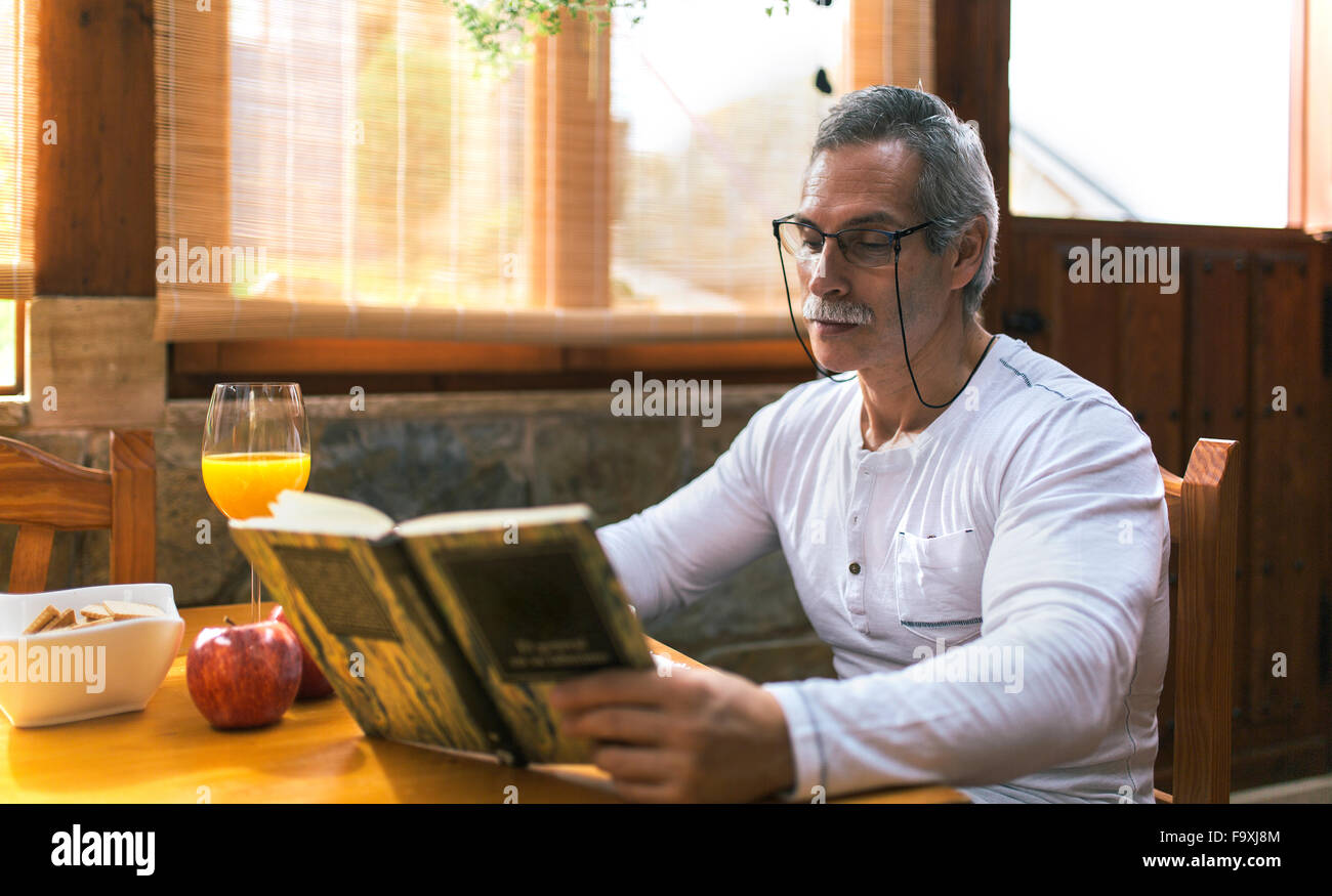 Man sitting at breakfast table reading a book Stock Photo - Alamy