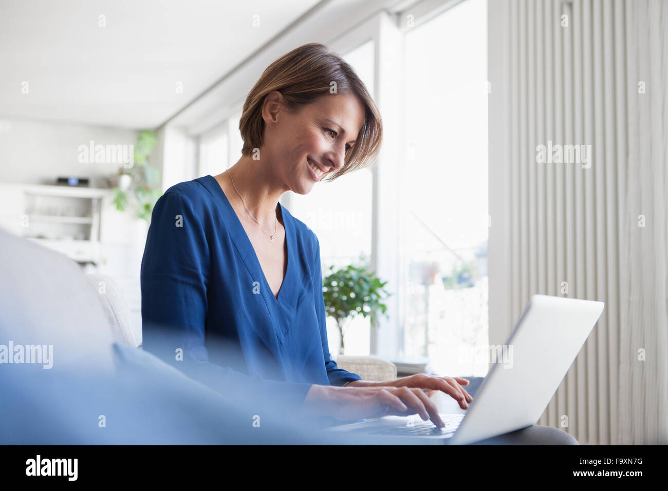 Smiling woman at home sitting on couch using laptop Stock Photo - Alamy