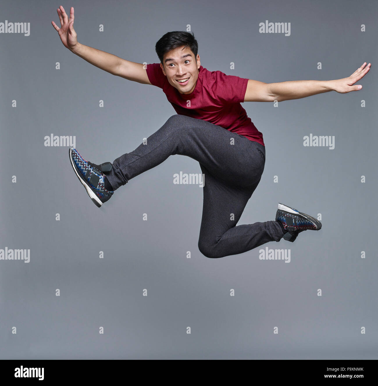 Portrait of young man jumping in the air in front of grey background ...