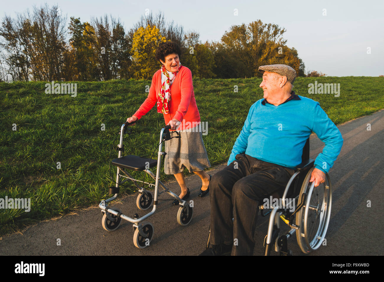 Smiling senior couple with wheelchair and wheeled walker on a path ...