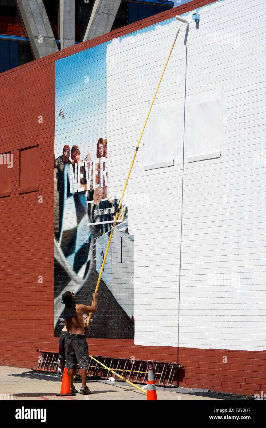 A man cleaning out an old advertising mural on a building wall in ...