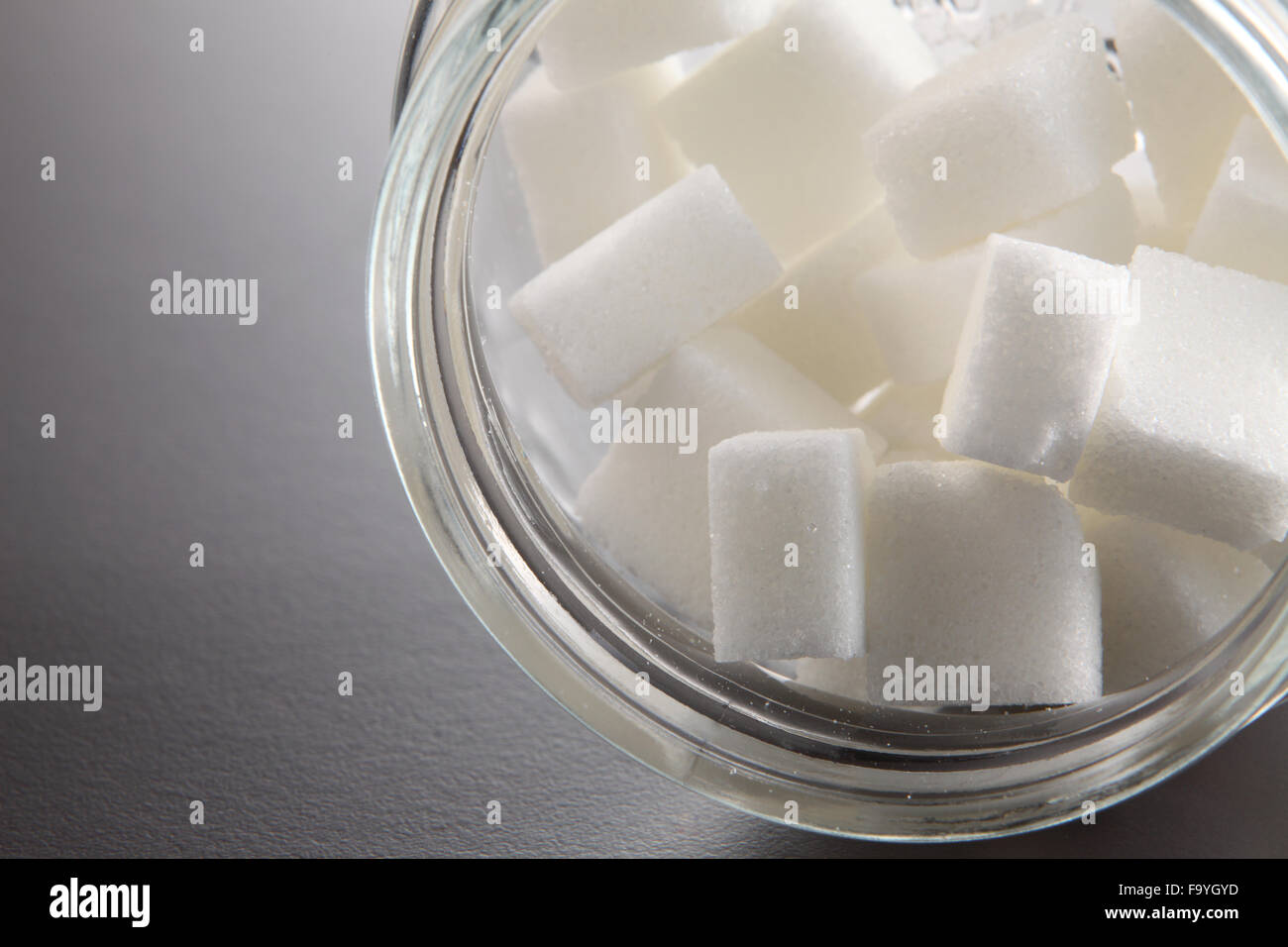 White lump sugar in a glass jar on a gray background, sweet sugar in ...