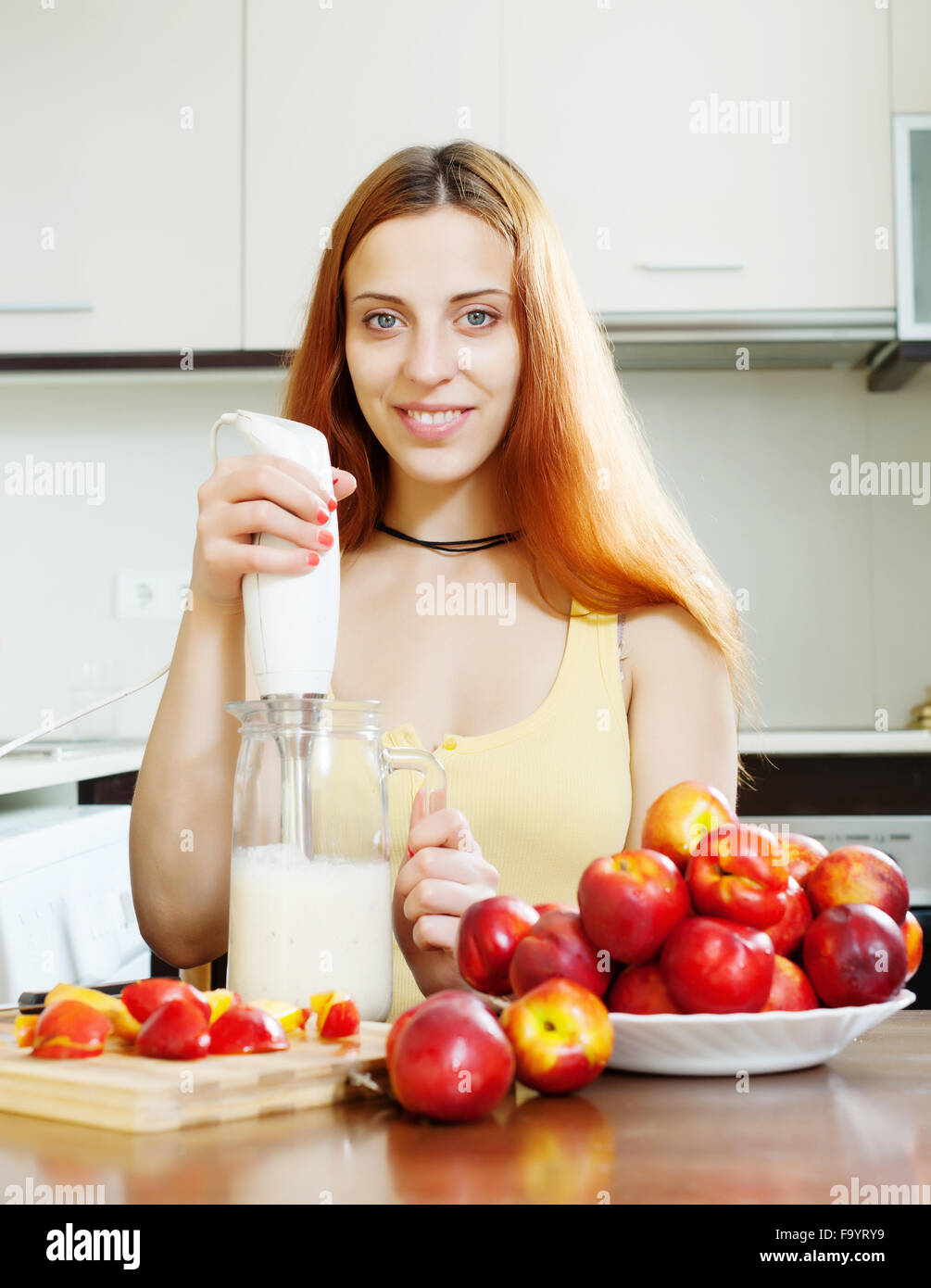 Positive long-haired woman making beverages with blender from ...