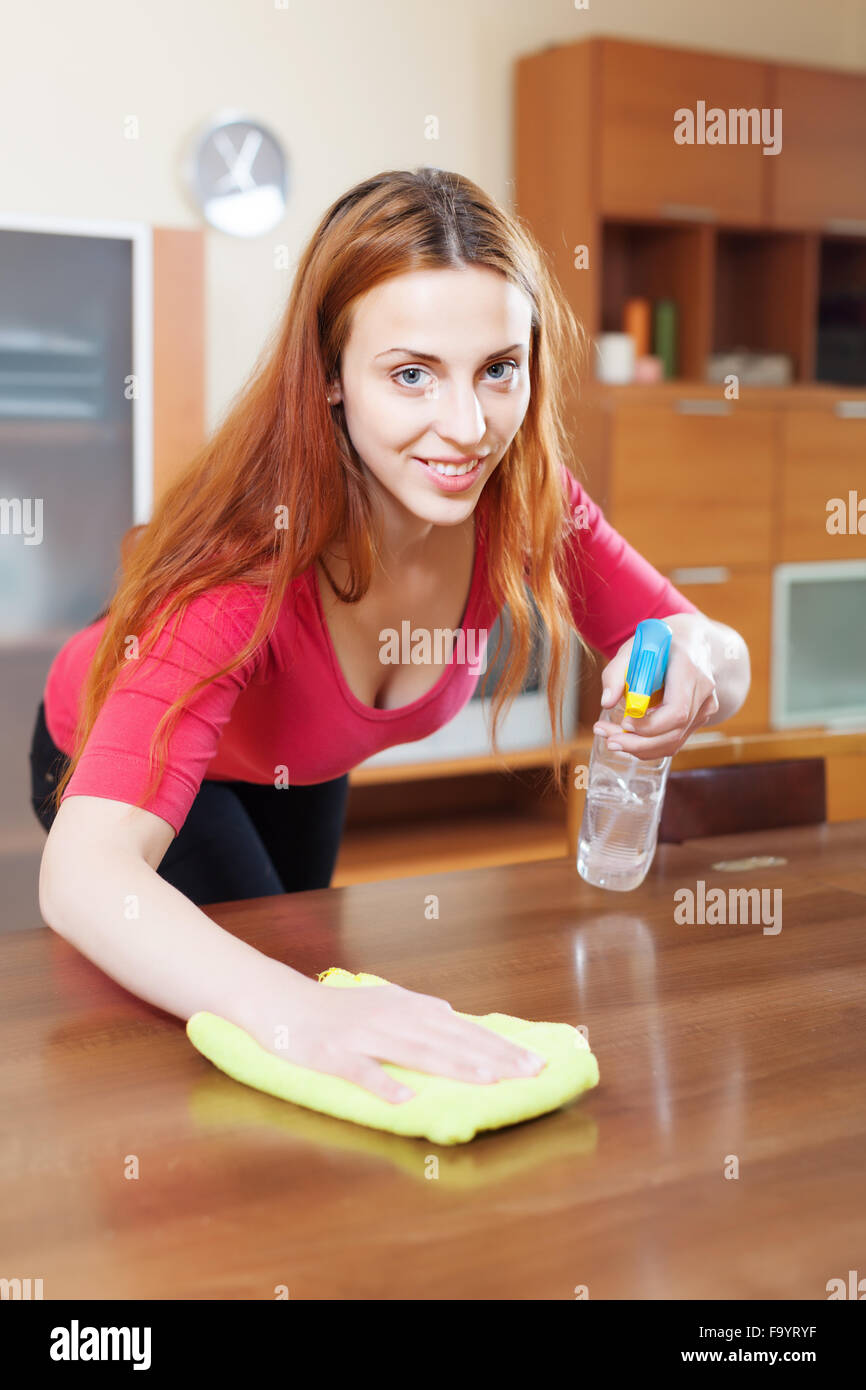 young woman dusting wooden table with rag and cleanser at home Stock ...