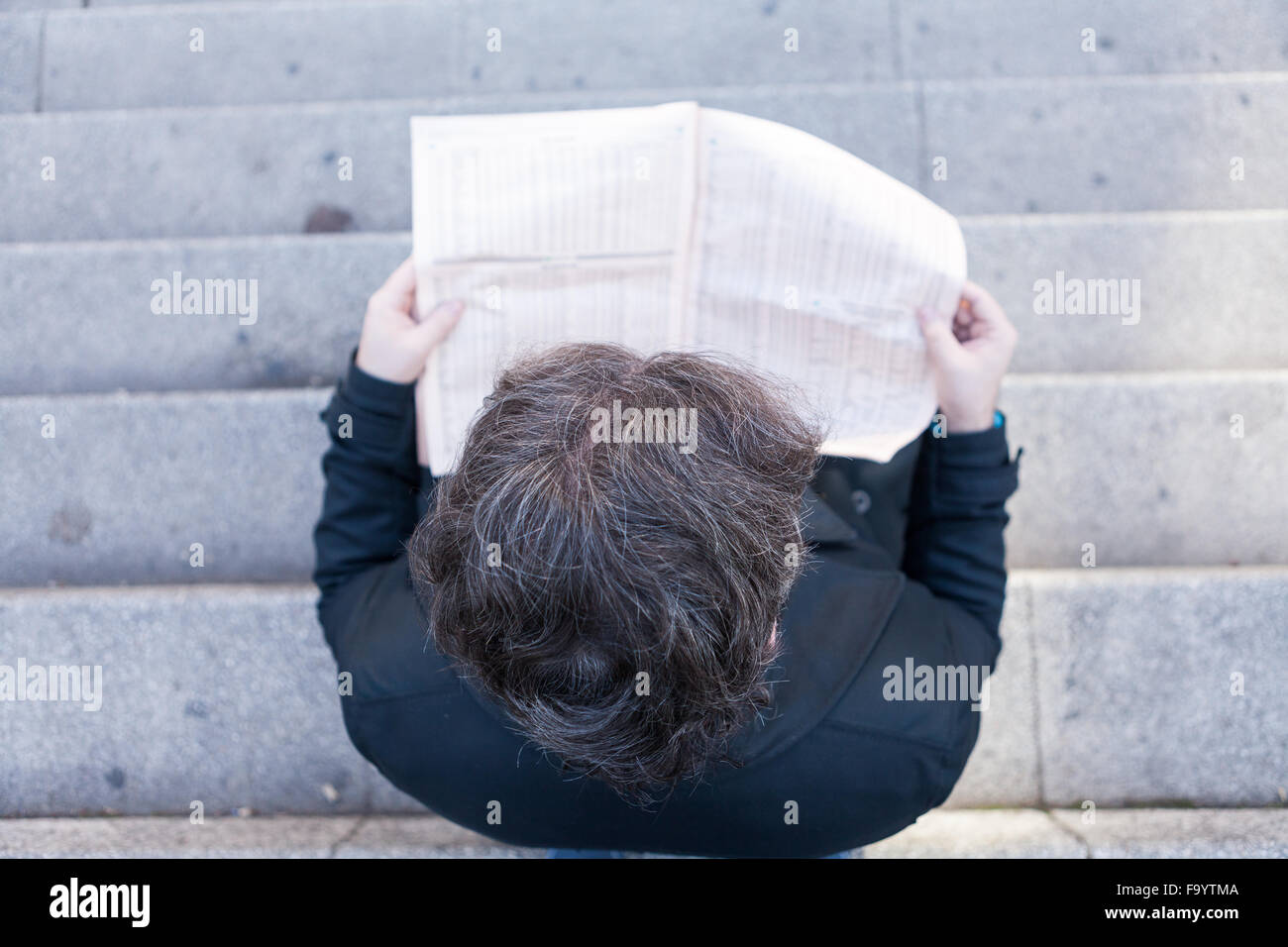 A young businessman with glasses reading a newspaper is thinking in ...