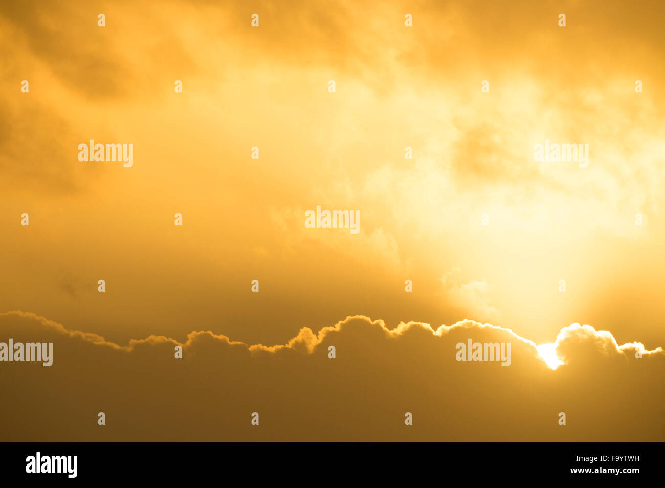 The golden light of the sun shining out from behind clouds Stock Photo ...