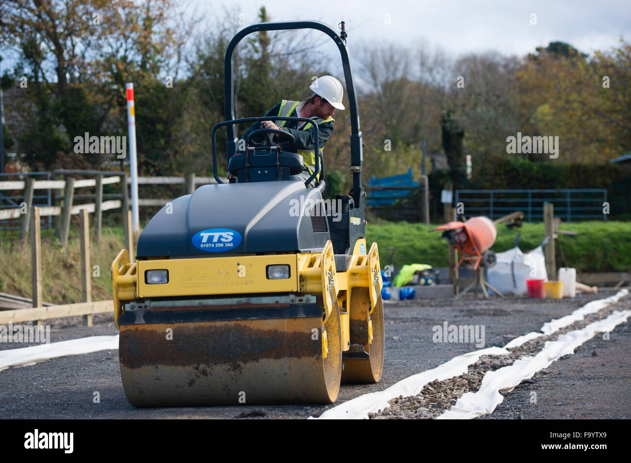 A man at work operating driving a yellow heavy roller plant machinery ...