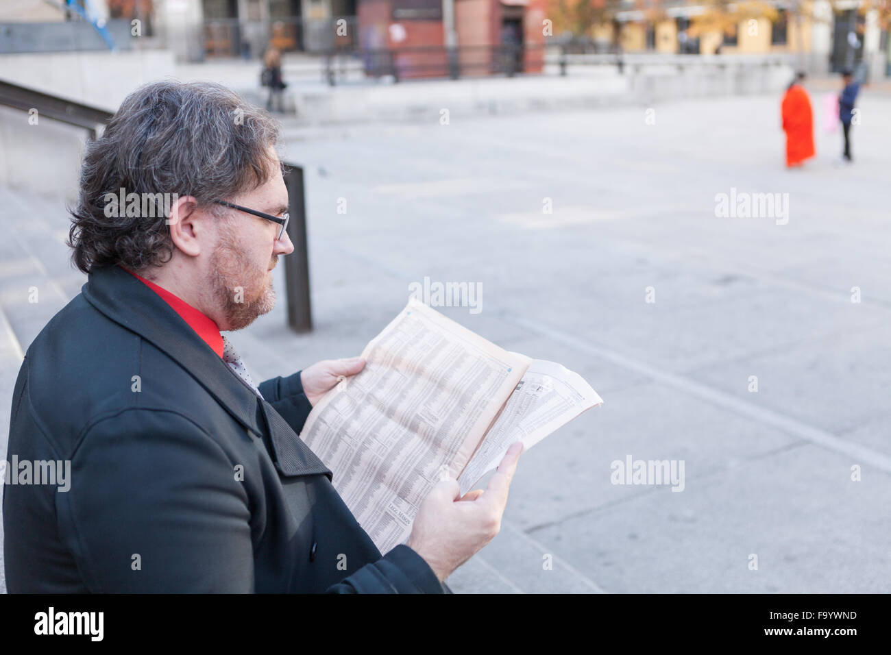 A young businessman with glasses reading a newspaper is thinking in ...