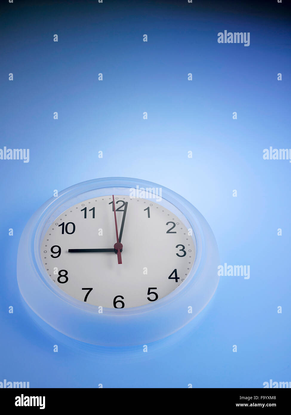 Clock showing 9 o'clock on a blue wall Stock Photo - Alamy