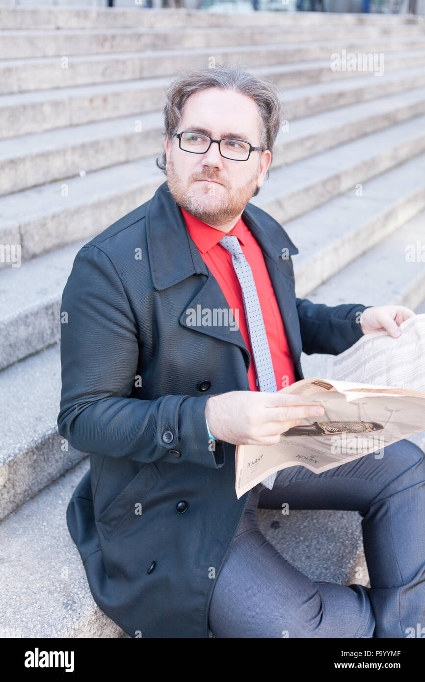 A young businessman with glasses reading a newspaper is thinking in ...