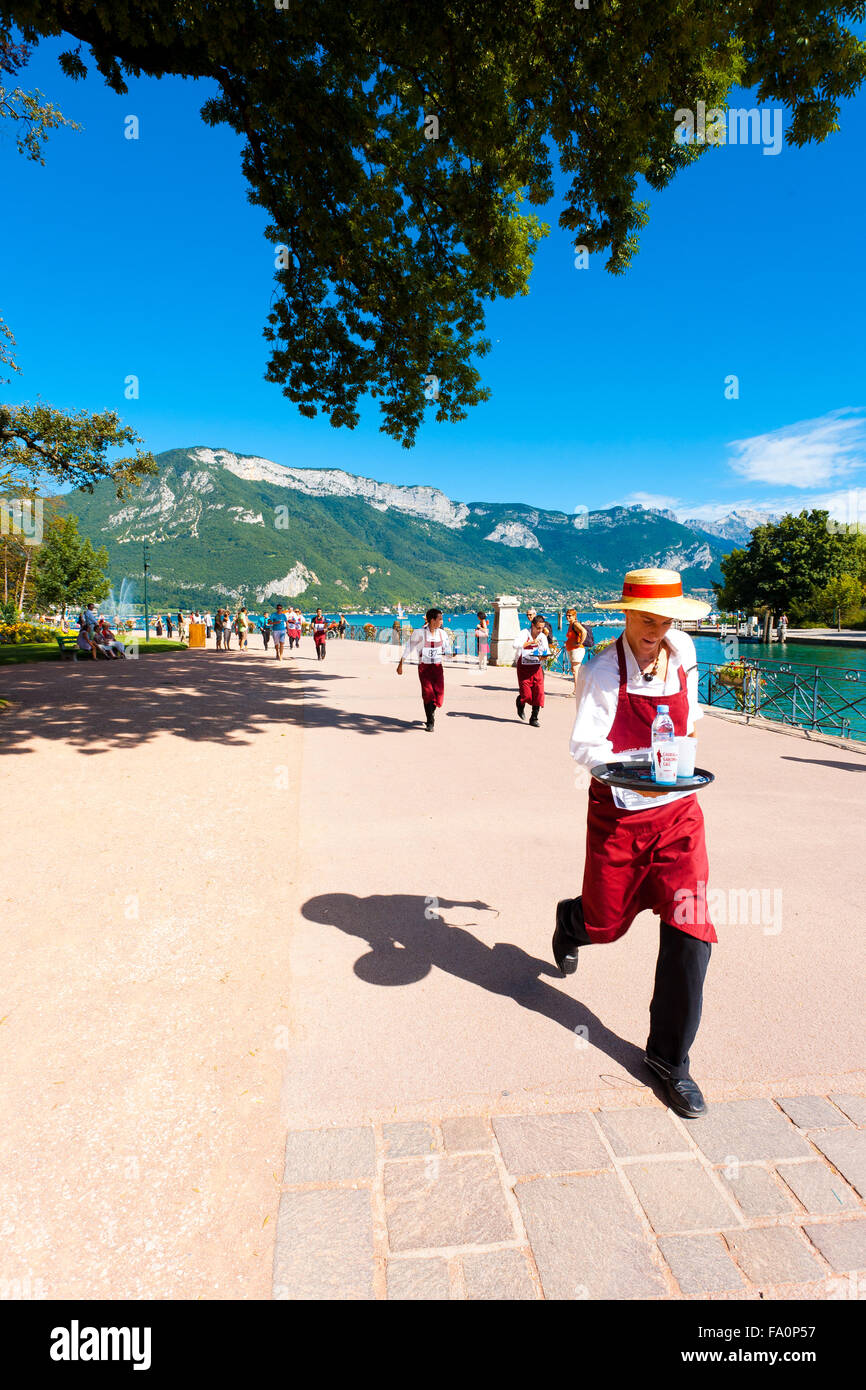 An apron wearing waiter runs with a loaded tray around Annecy Lake at ...