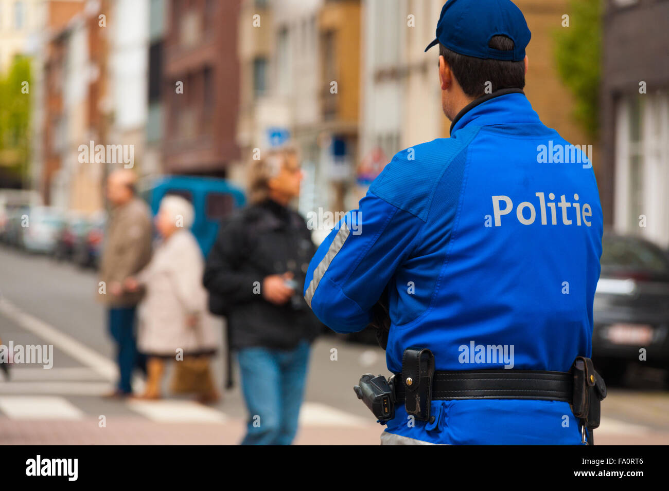Rear of Flemish Policeman in blue Politie jacket, hat watching ...