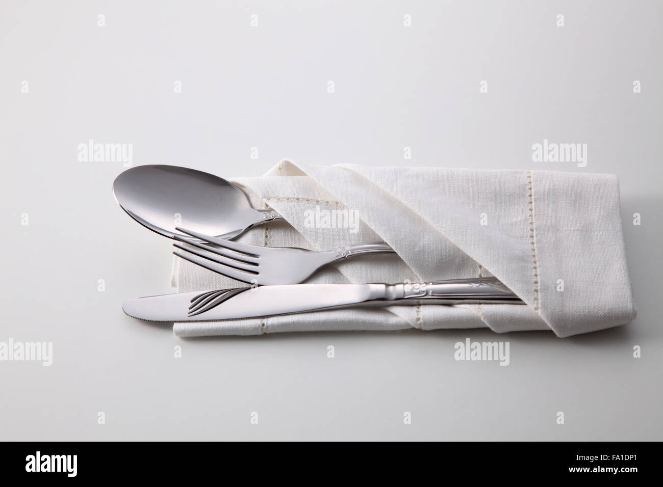 Folded napkin with fork, spoon and knife on white background Stock ...