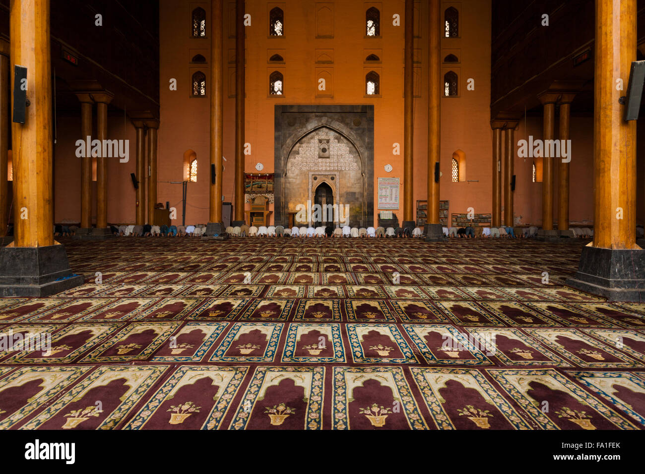 A row of muslims praying, bowing head touching floor facing a wall in ...