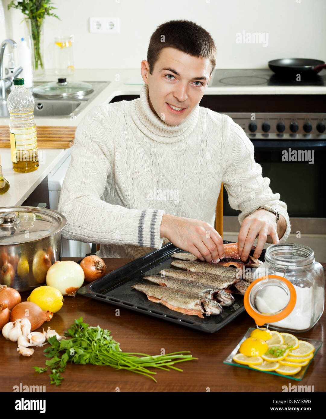 Happy man putting saltwater fish into sheet pan at kitchen table Stock ...