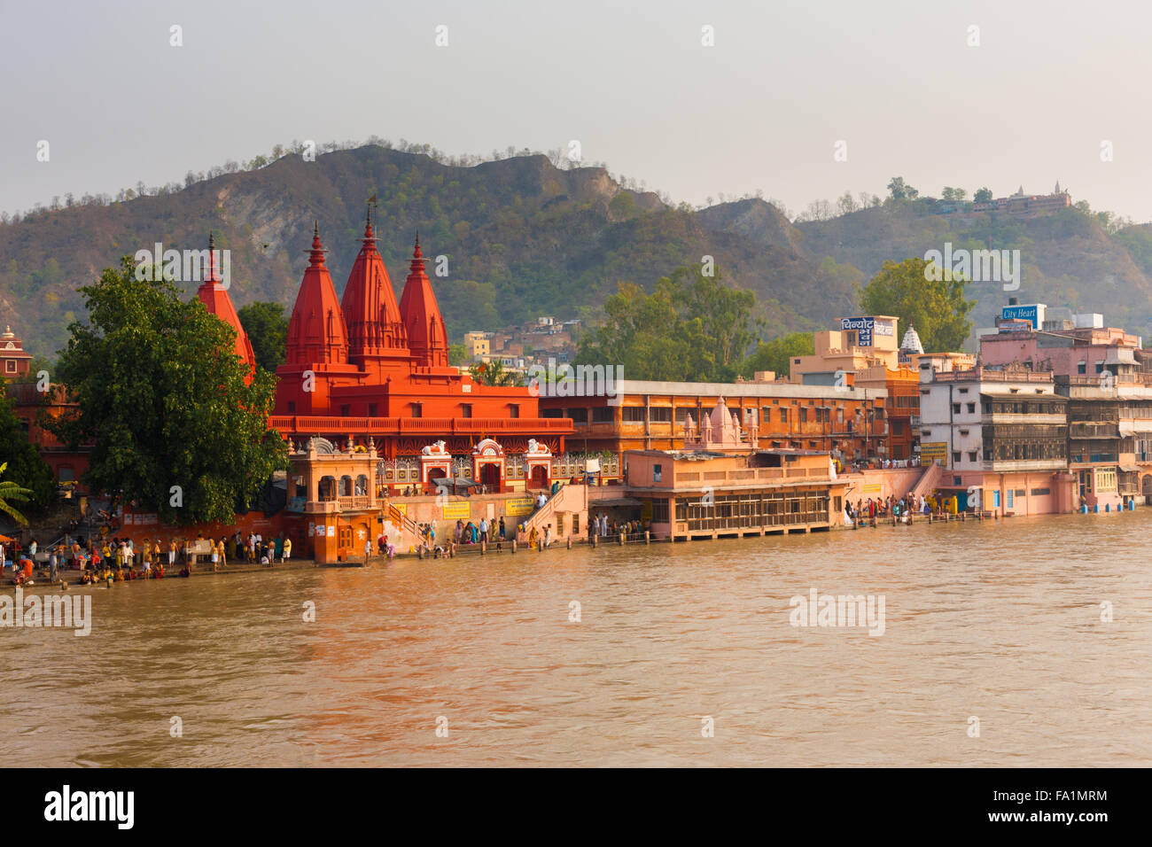 Hindus gathering at a pilgrimage spot near a red temple for bathing and ...