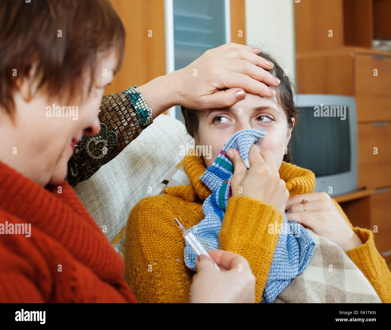 Mature woman caring for her adult daughter has cold in living room ...