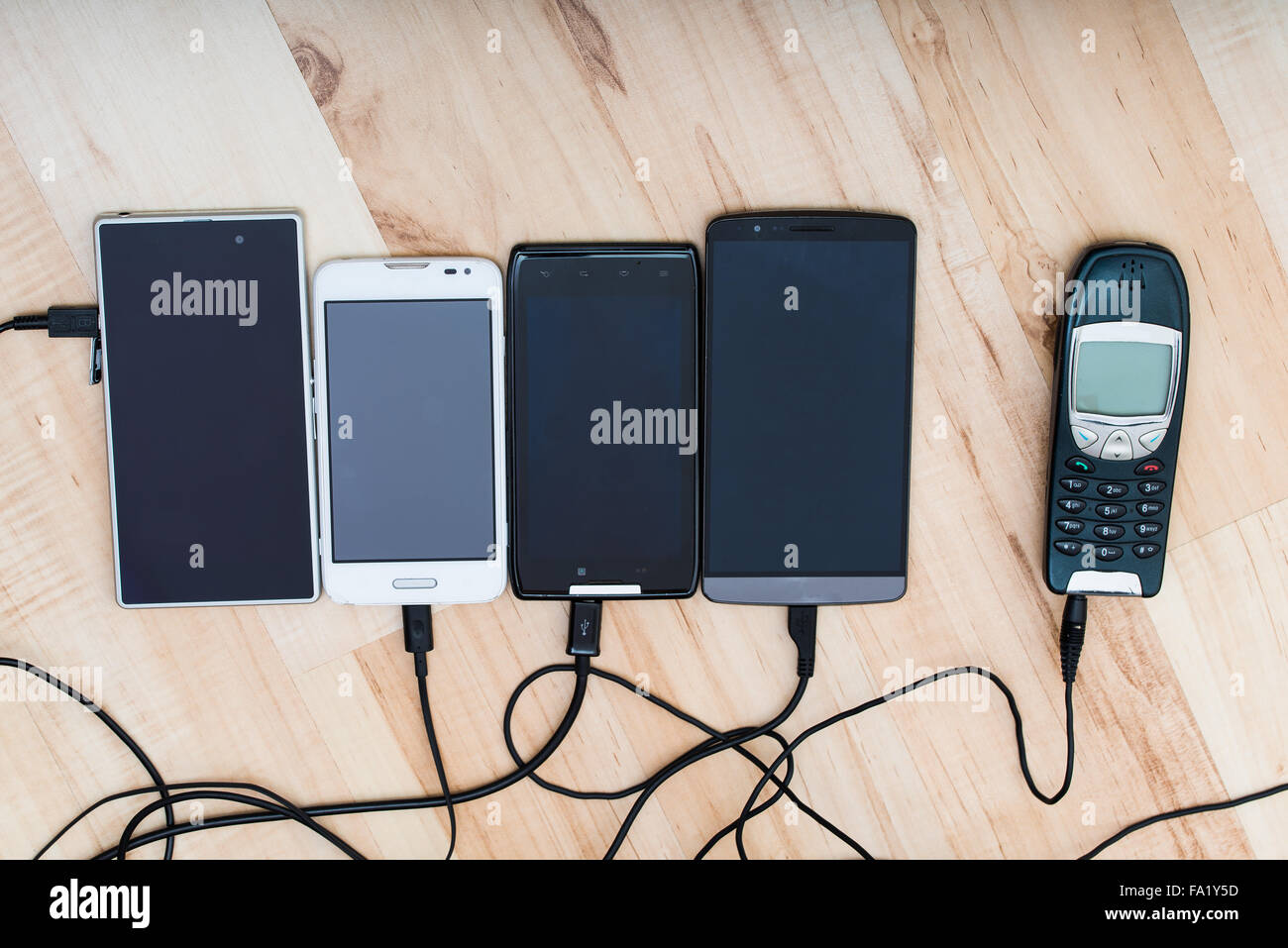 four smartphones and one classic phone connected to chargers Stock ...