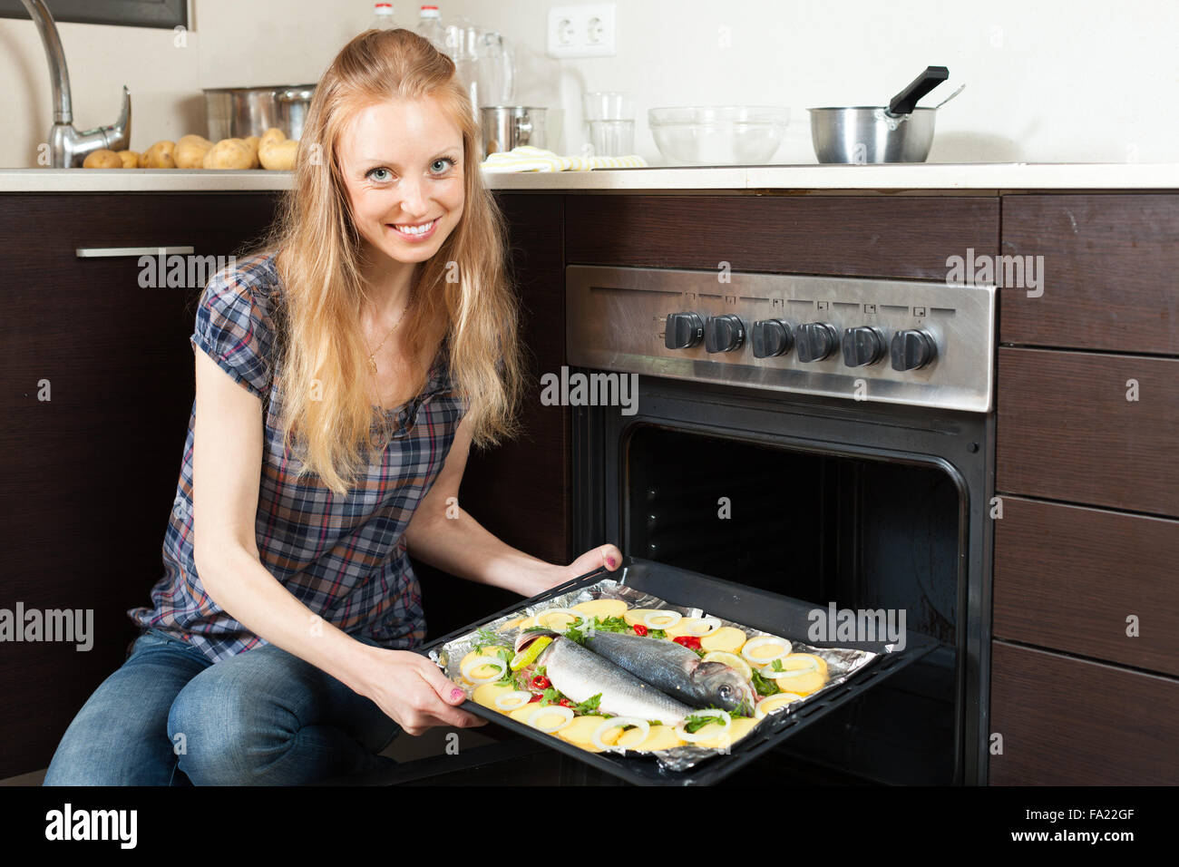 Smiling girl cooking raw fish in oven at kitchen Stock Photo - Alamy