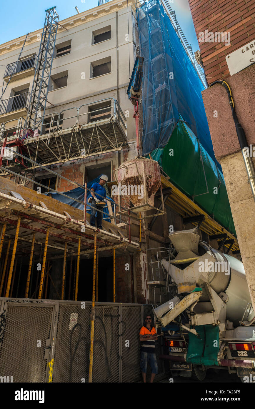 Worker running a construction crane is lifting a container of cement in ...