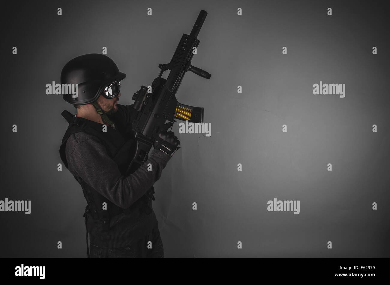 airsoft player with gun, helmet and bulletproof vest on gray background ...
