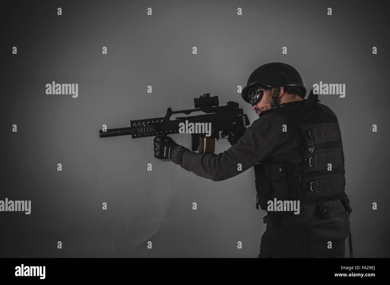 airsoft player with gun, helmet and bulletproof vest on gray background ...