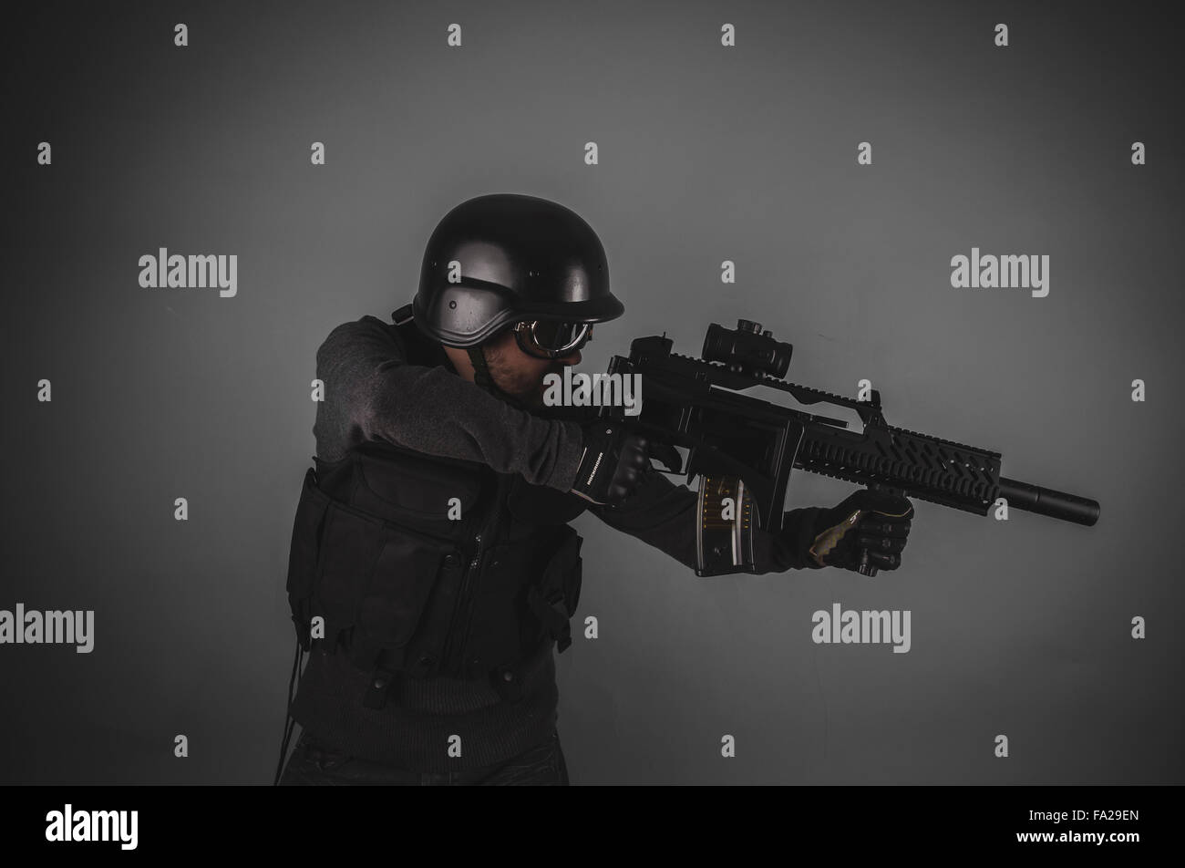 airsoft player with gun, helmet and bulletproof vest on gray background ...