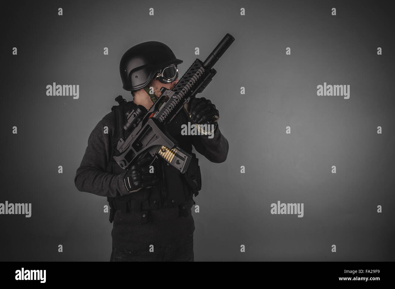 aiming, airsoft player with gun, helmet and bulletproof vest on gray ...