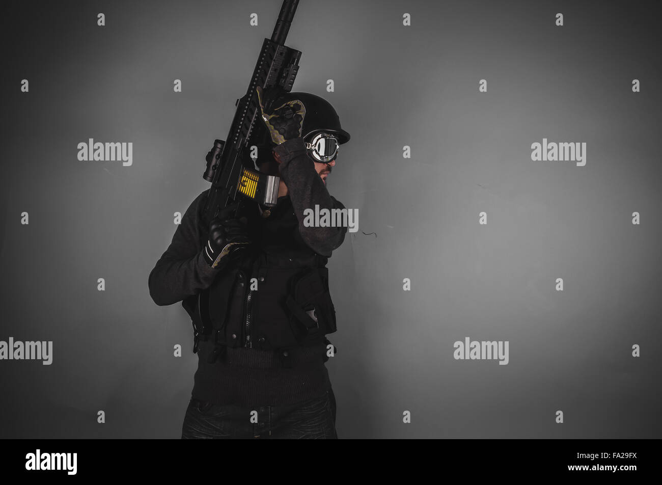 airsoft player with gun, helmet and bulletproof vest on gray background ...