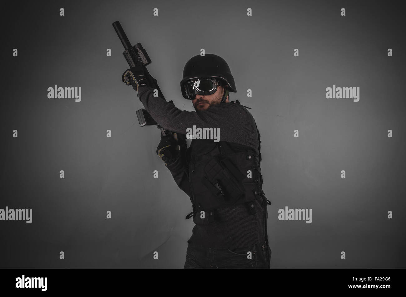 airsoft player with gun, helmet and bulletproof vest on gray background ...