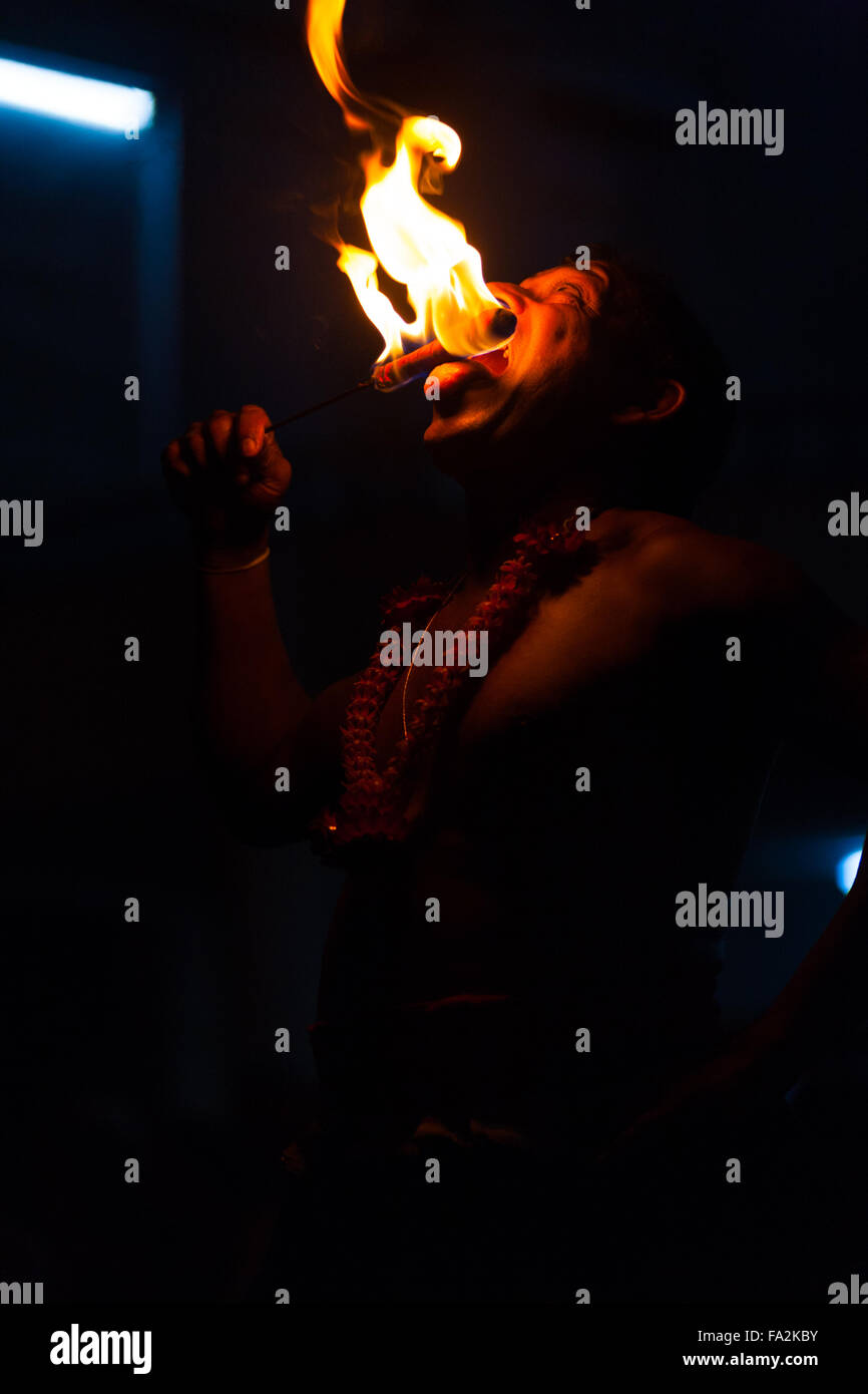 A shirtless man touching a flaming stick to tongue, mouth during a ...