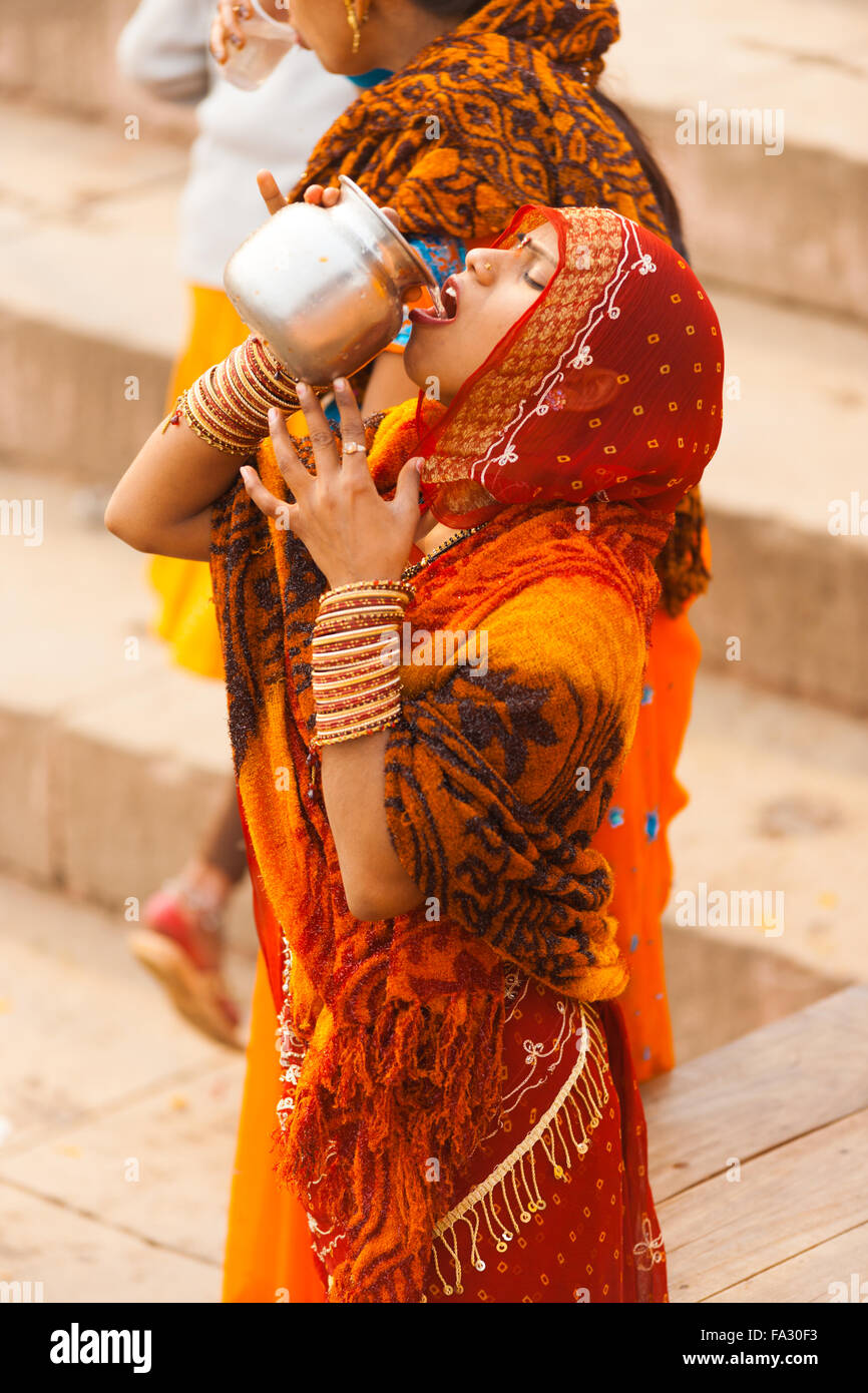 A young Indian woman in red saree pouring into mouth, drinking ...