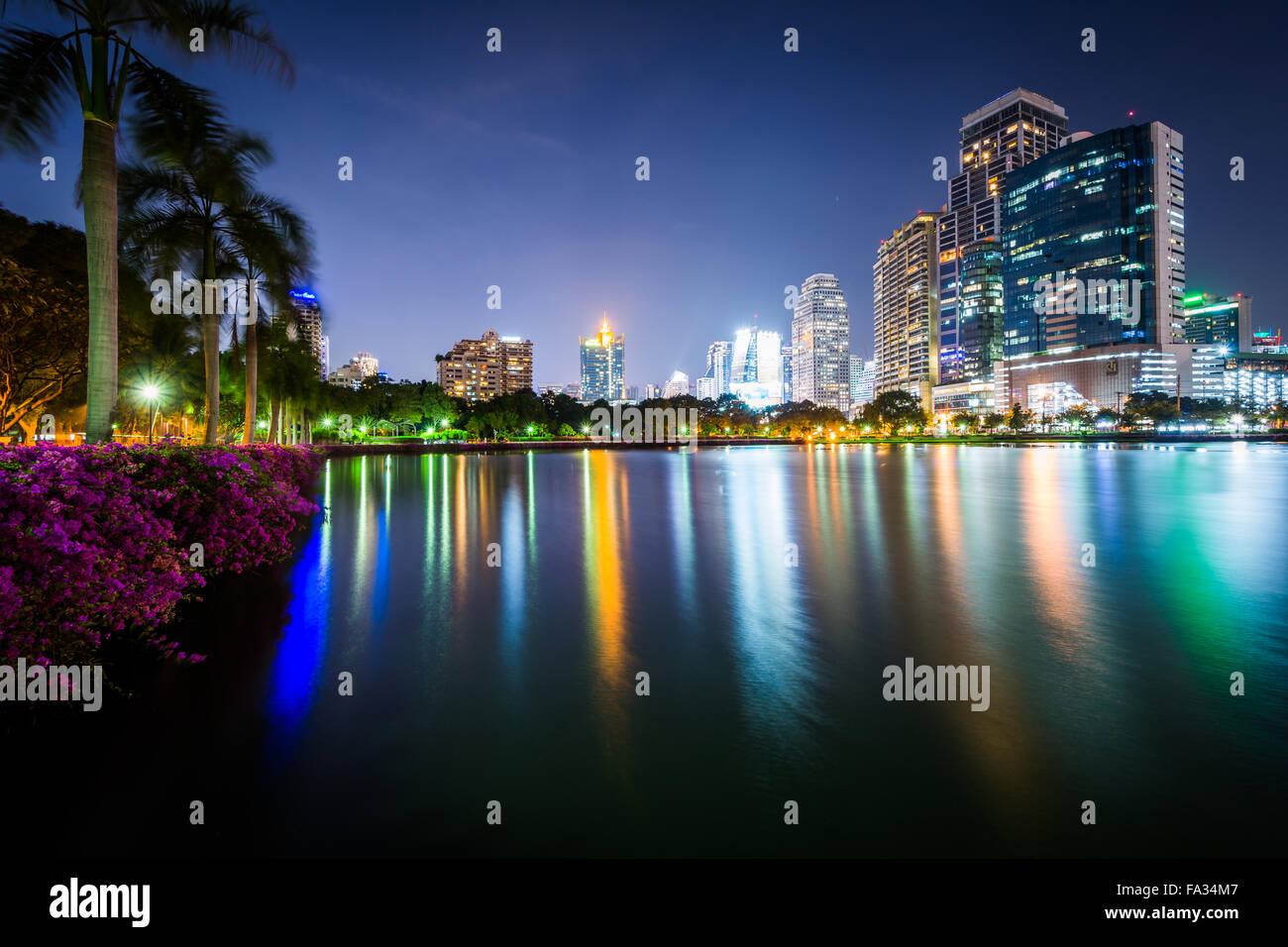 Modern skyscrapers and palm trees along Lake Rajada at night, at ...