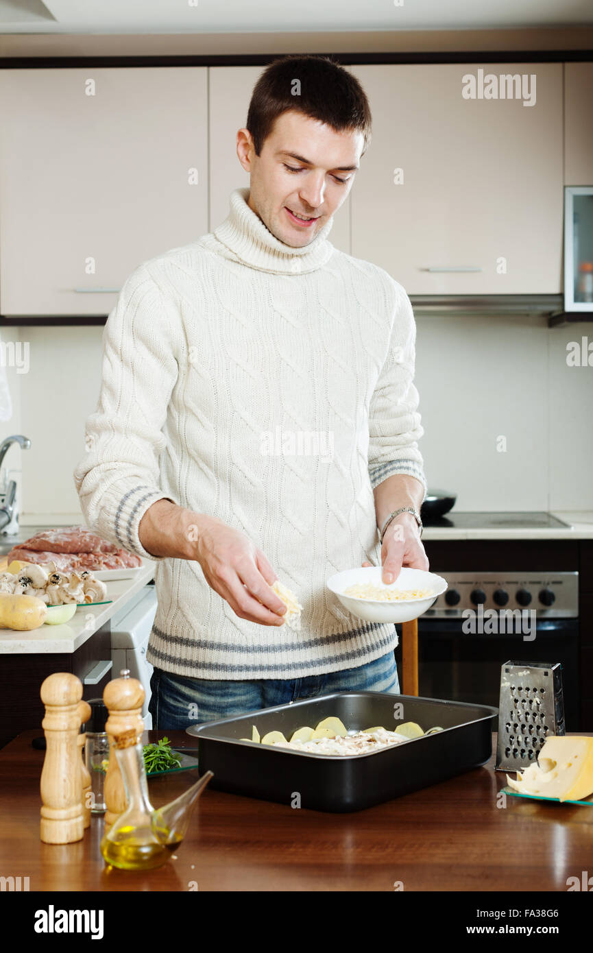 Handsome man cooking french-style meat. Adding grated cheese in ...