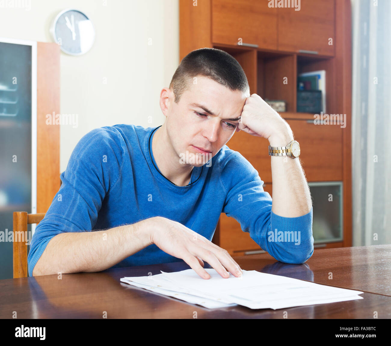 Sad young man looking at financial documents in frustration sitting at ...