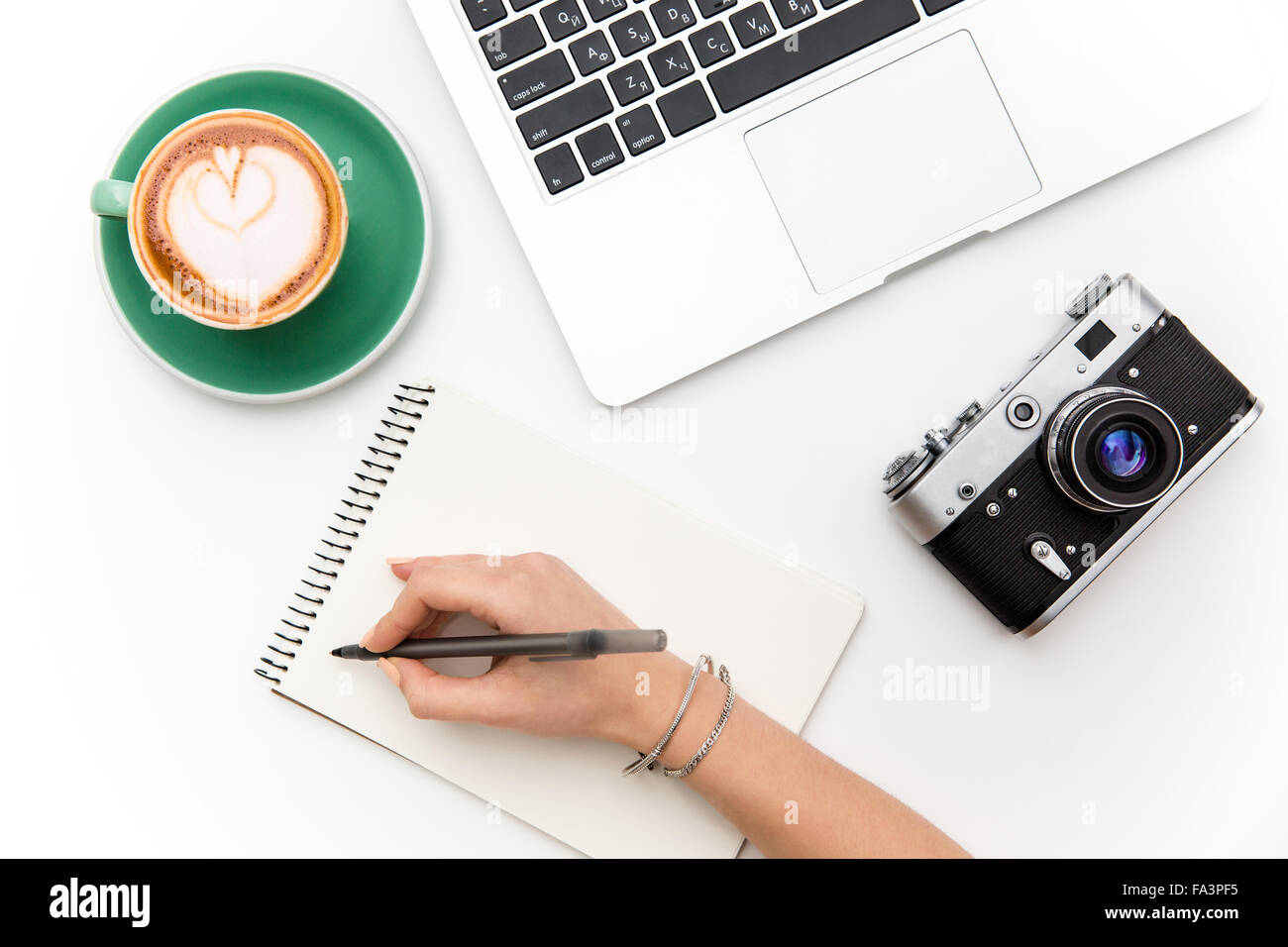 Top view of laptop, old camera, cup of coffee and woman hand writing in ...