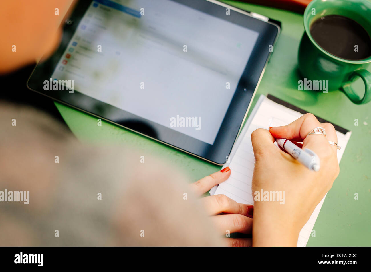 Over the shoulder view of woman with digital tablet writing on notepad ...