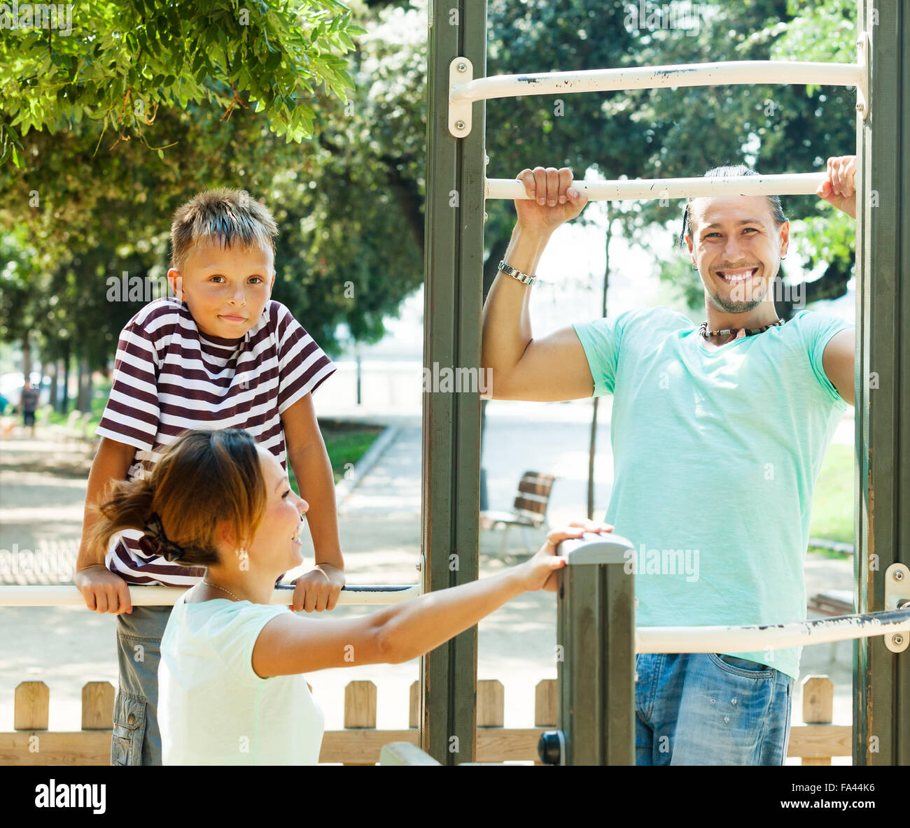Middle-aged man with family training on chin-up bar at yard in summer ...
