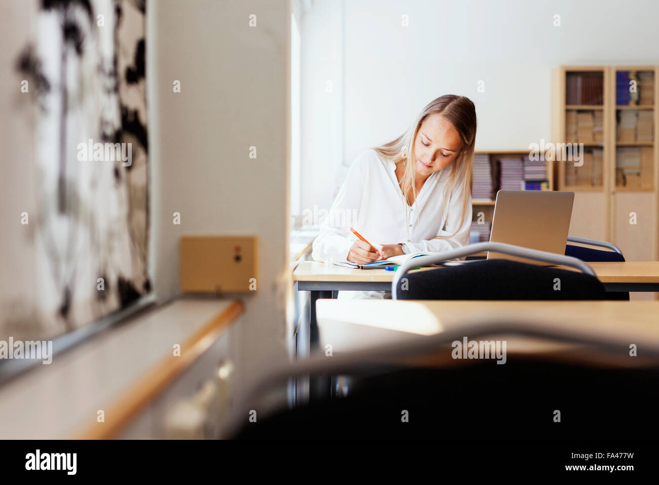 Young woman writing at desk in classroom Stock Photo - Alamy