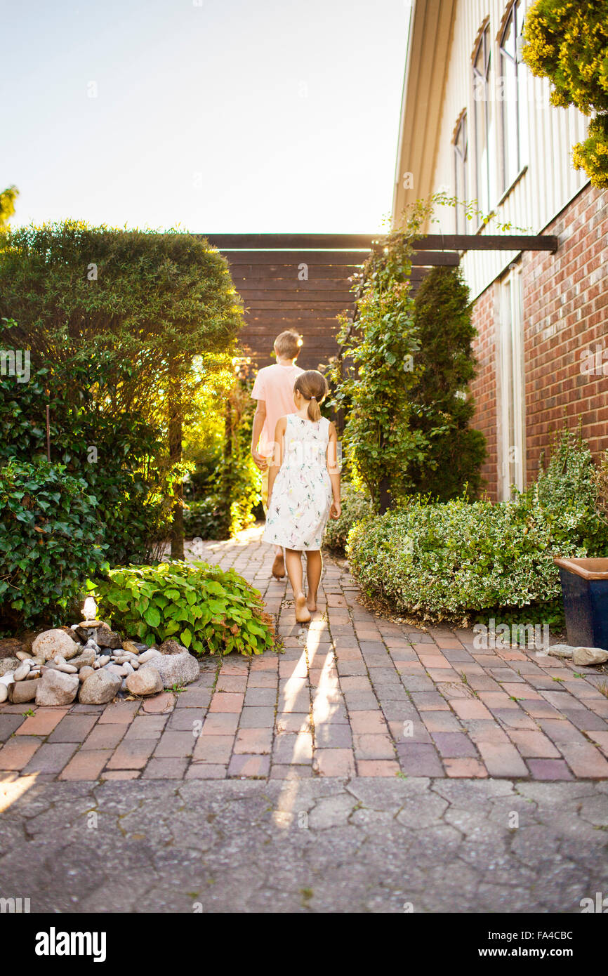 Rear view of brother and sister walking in garden Stock Photo - Alamy